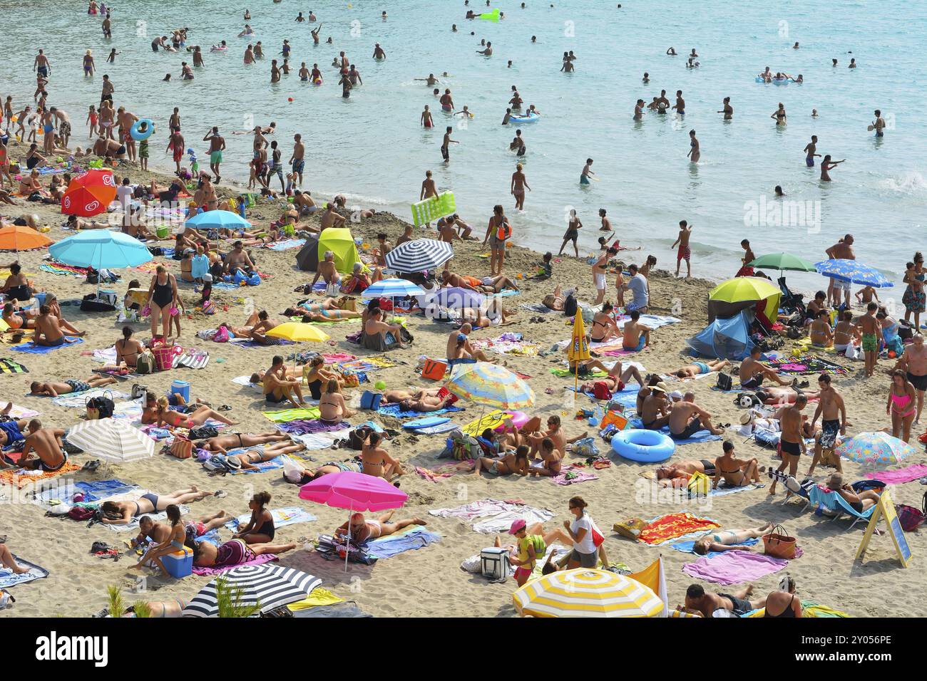 A crowded beach with many people sunbathing and swimming, colorful ...