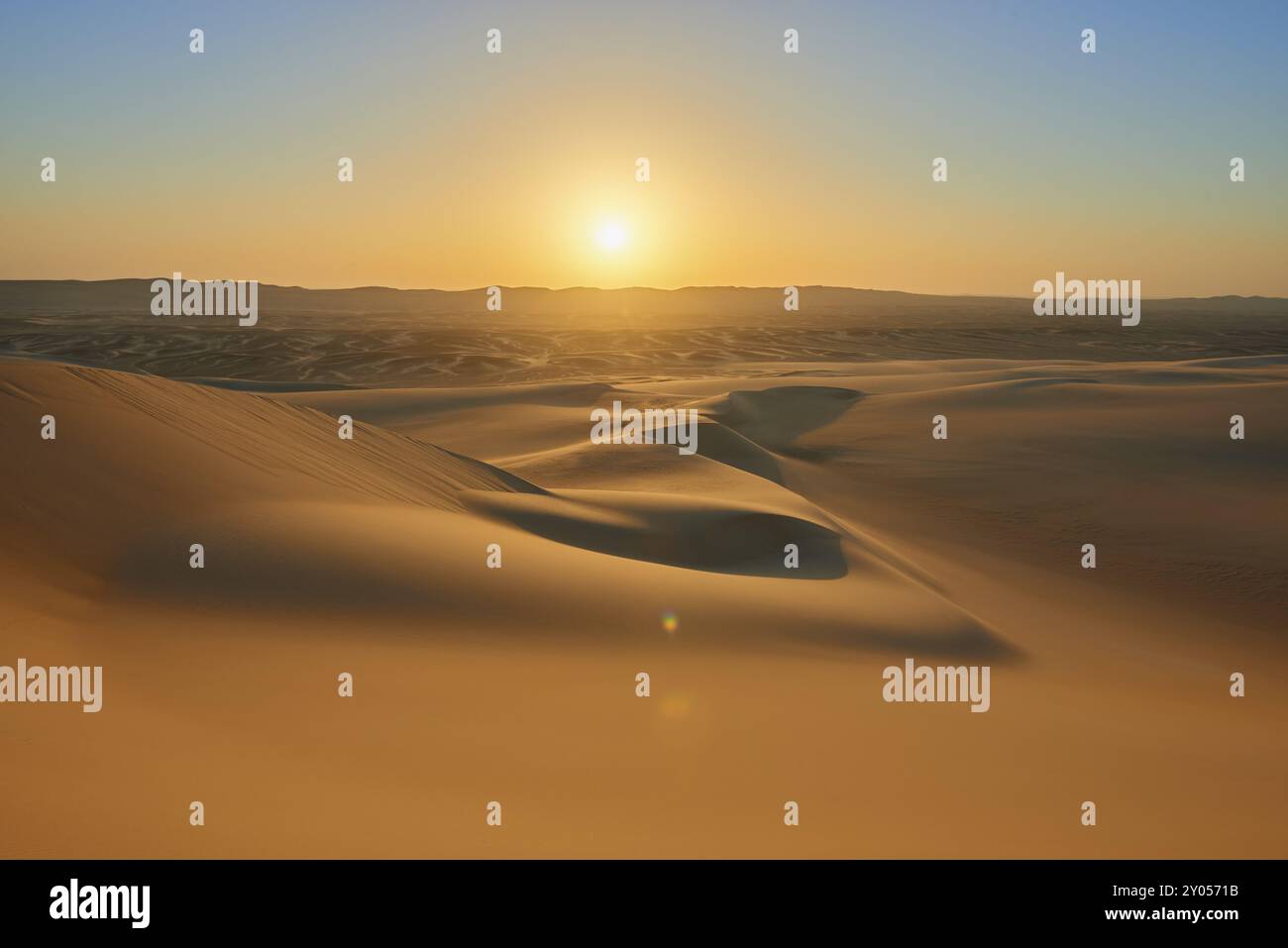 Sunset over a vast desert landscape with gentle sand dunes and clear ...