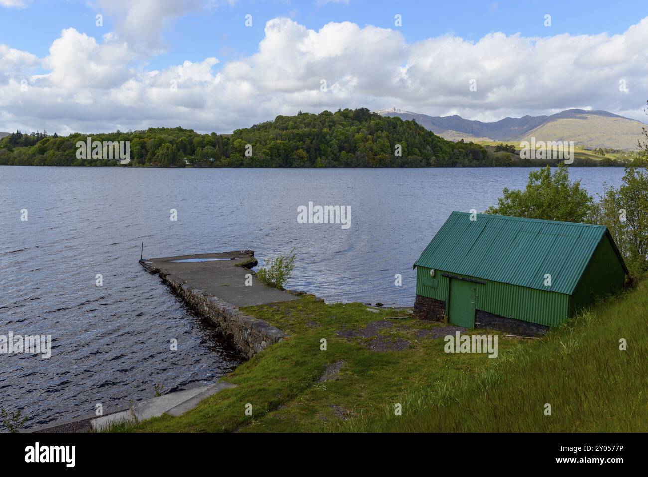 A scenic lake view with a green shed beside a dock, surrounded by hills ...