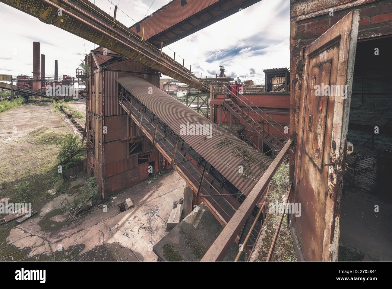 Abandoned factory full of rusty structures, plants surround the area ...