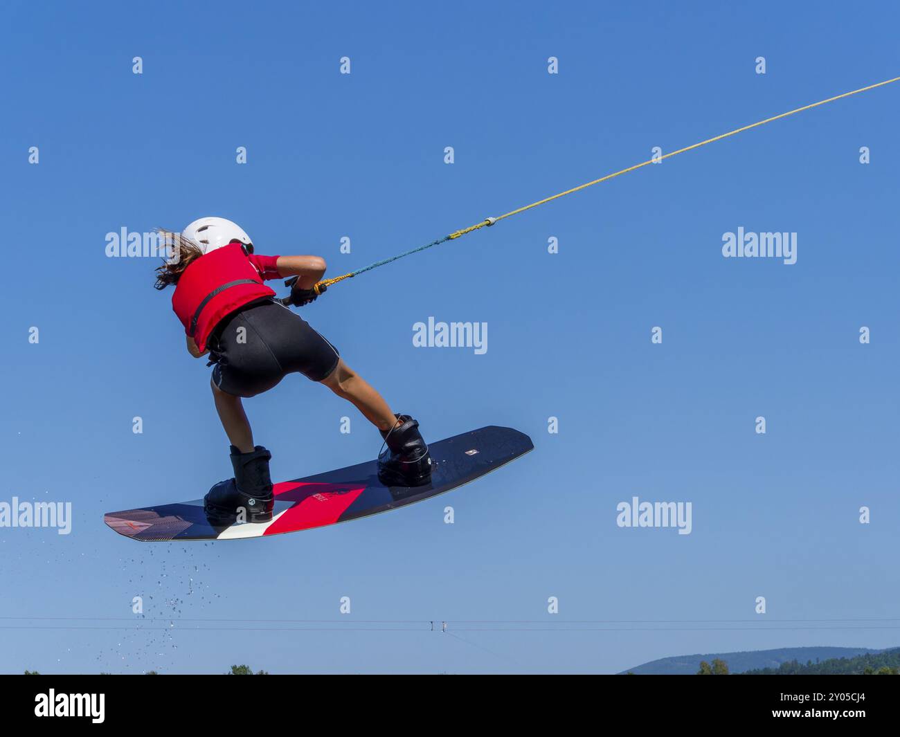 Boy or girl, jump with wakeboard over the lake, red life jacket and ...