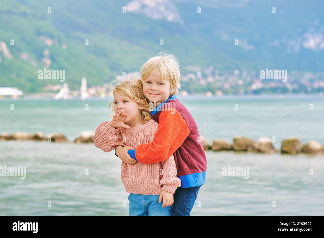 Outdoor portrait of 2 adorable kids hugging each other, posing next to ...