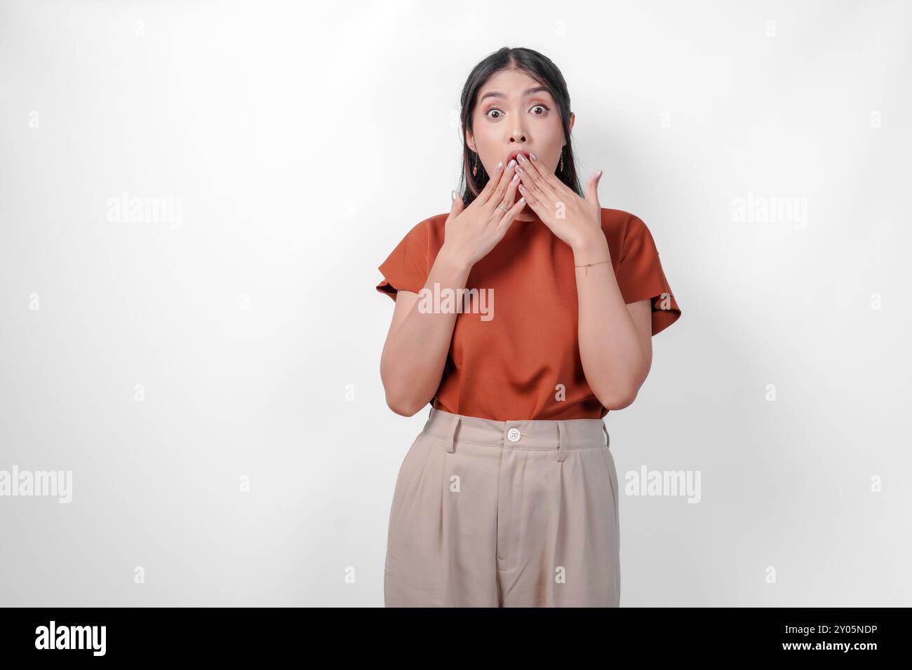 Surprised young Asian woman in a brown shirt and taupe pants is looking ...