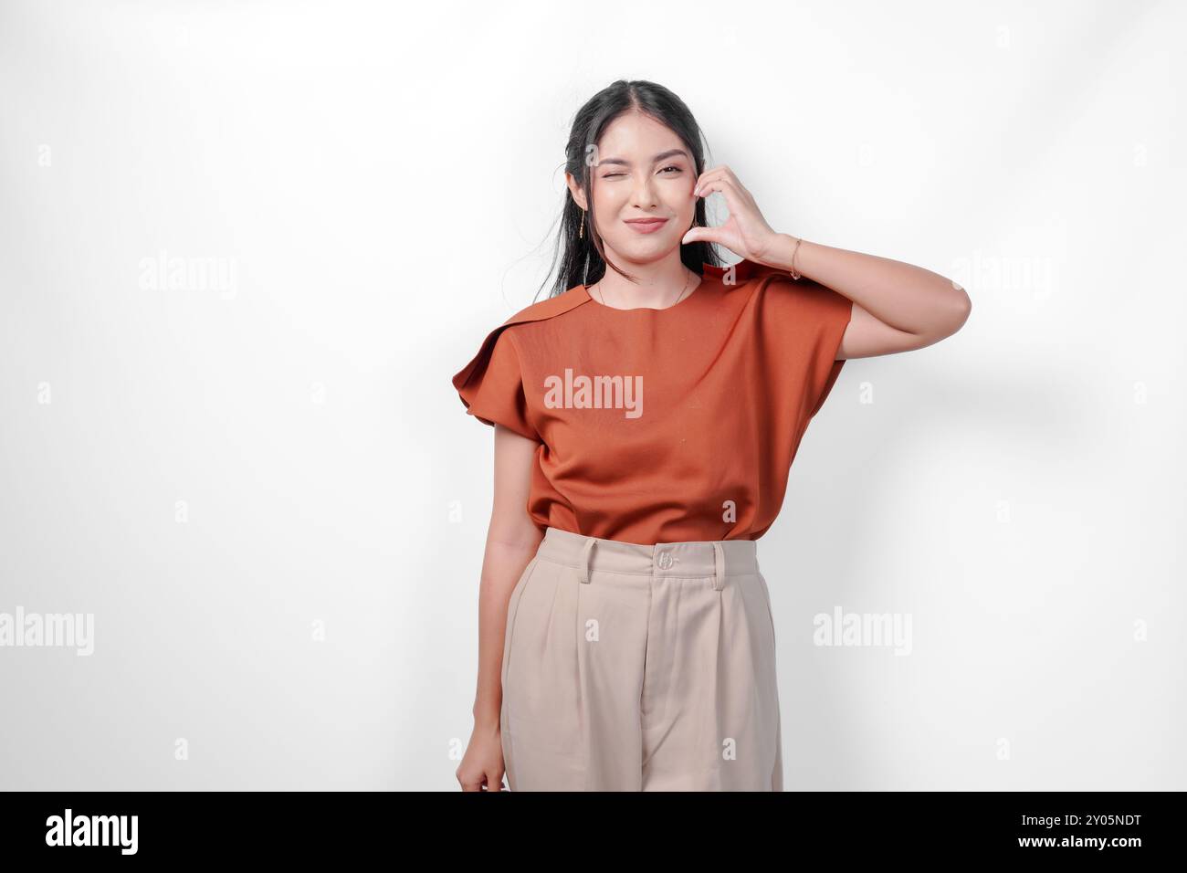 Cute young Asian woman in a brown shirt making a heart gesture on her ...