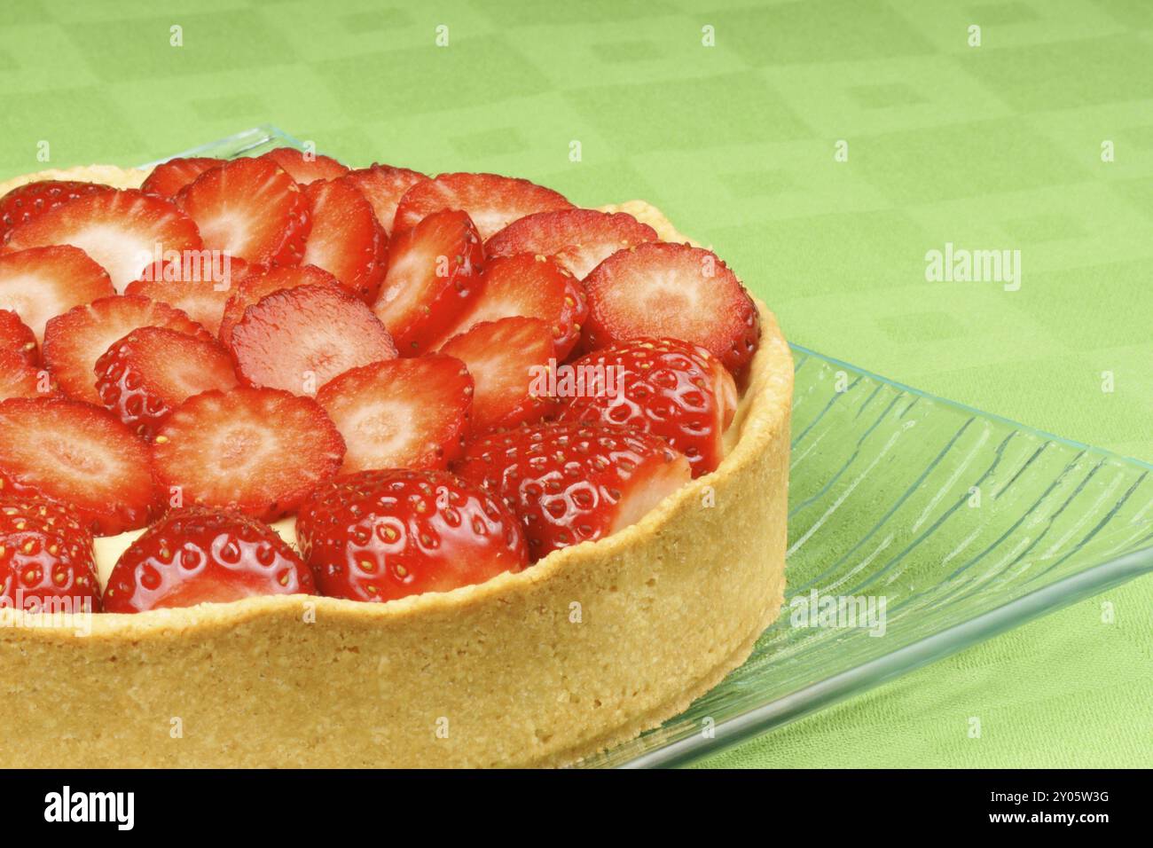 Strawberry and custard tart on a transparent glass dish over a green ...