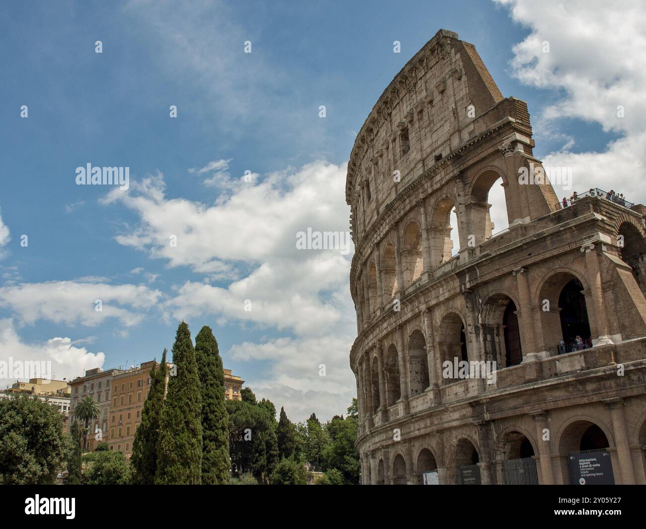 Impressive Colosseum with arcades and cloudy sky, trees and buildings ...