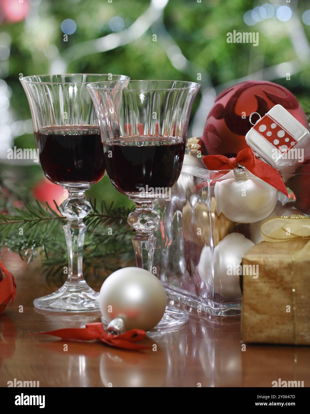 Glasses of red wine and balls in front of Christmas tree for the ...