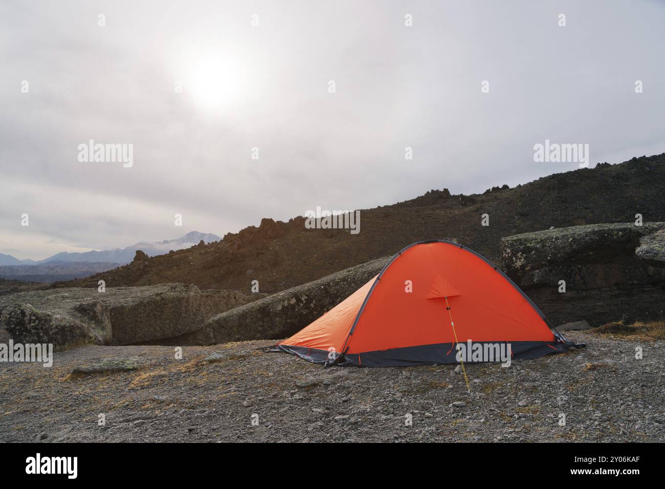 An orange high-altitude tent is set between stones high in the ...