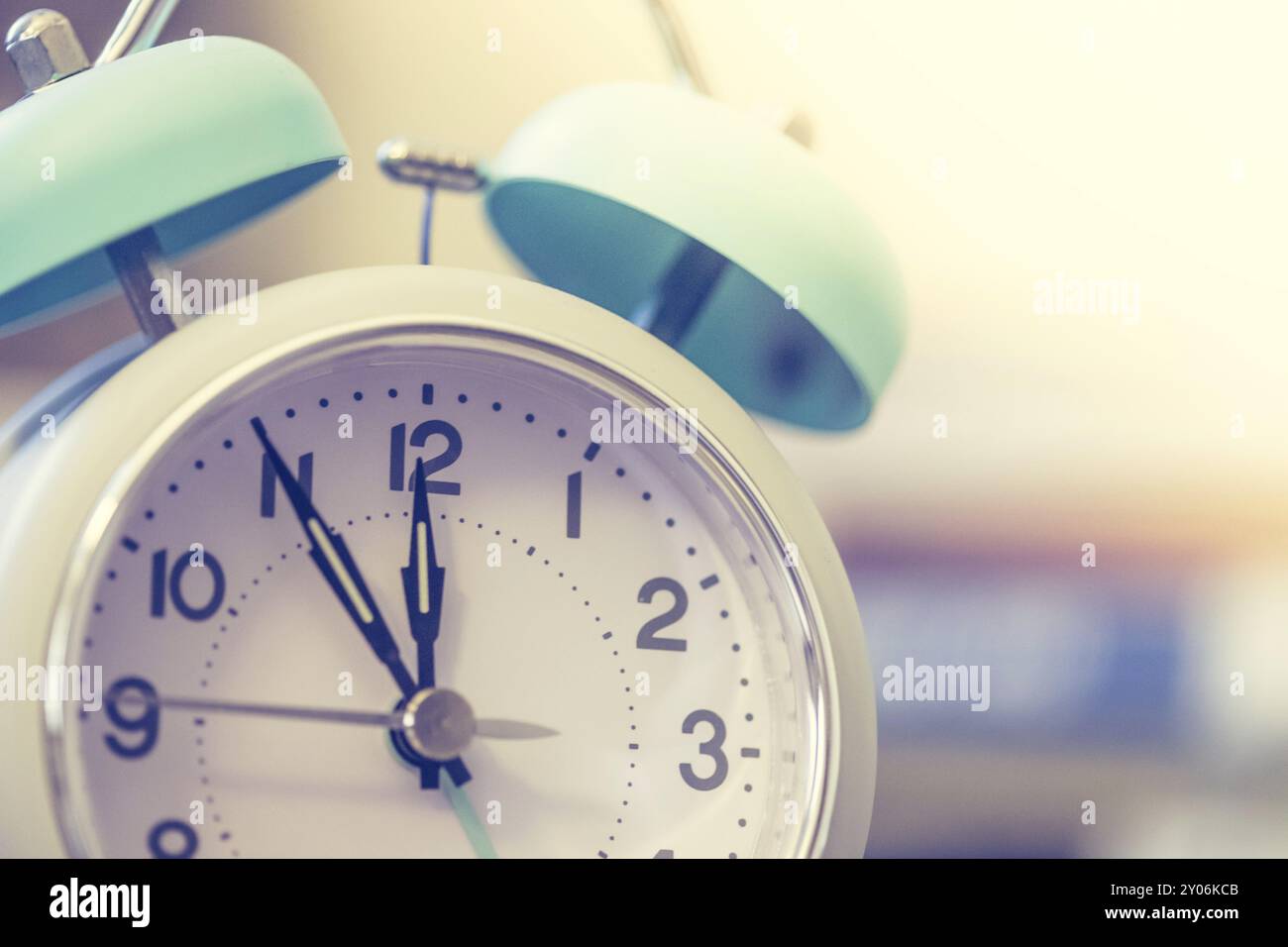 Alarm clock is standing on a grey desk, books in the blurry background ...