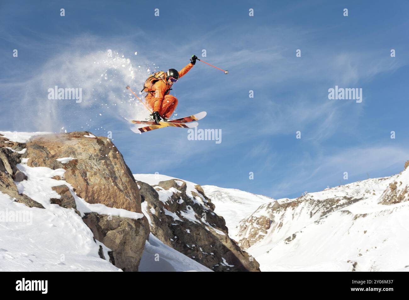 A professional skier makes a jump-drop from a high cliff against the ...