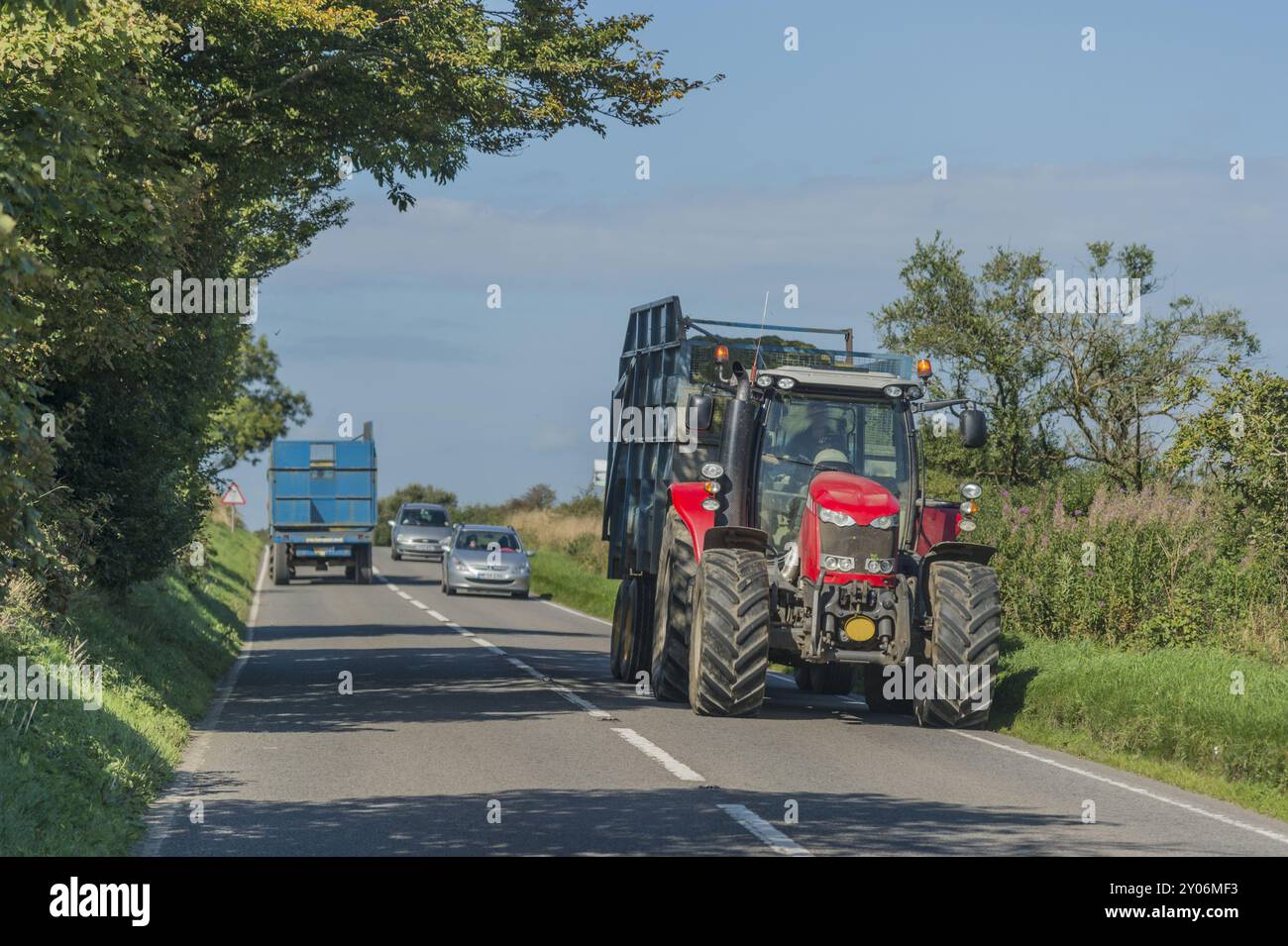 Red tractor with trailer on a country road in left-hand traffic Stock ...