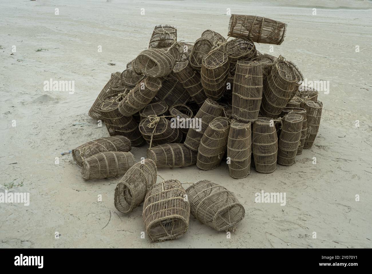 pile of empty, cylindrical wire crab traps on sandy surface, near ...