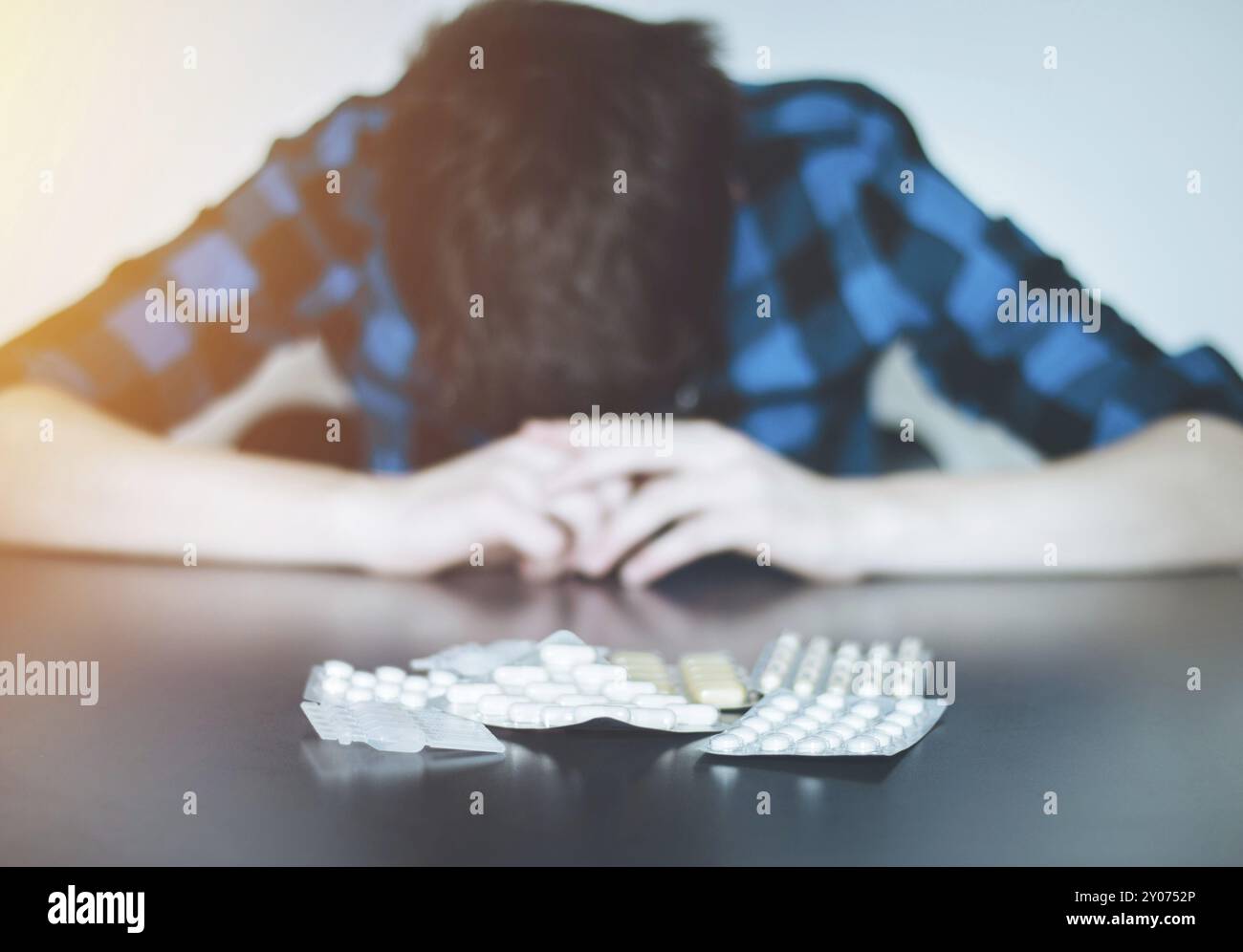 Drug abuse: Young man sitting on a table, drugs and pills in front of ...