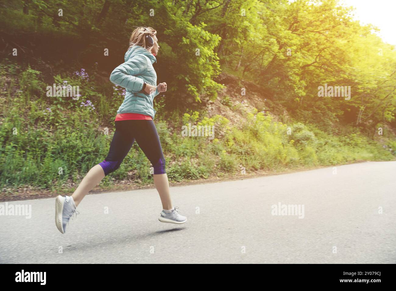 A young blonde woman running is practicing outdoors in a city mountain ...
