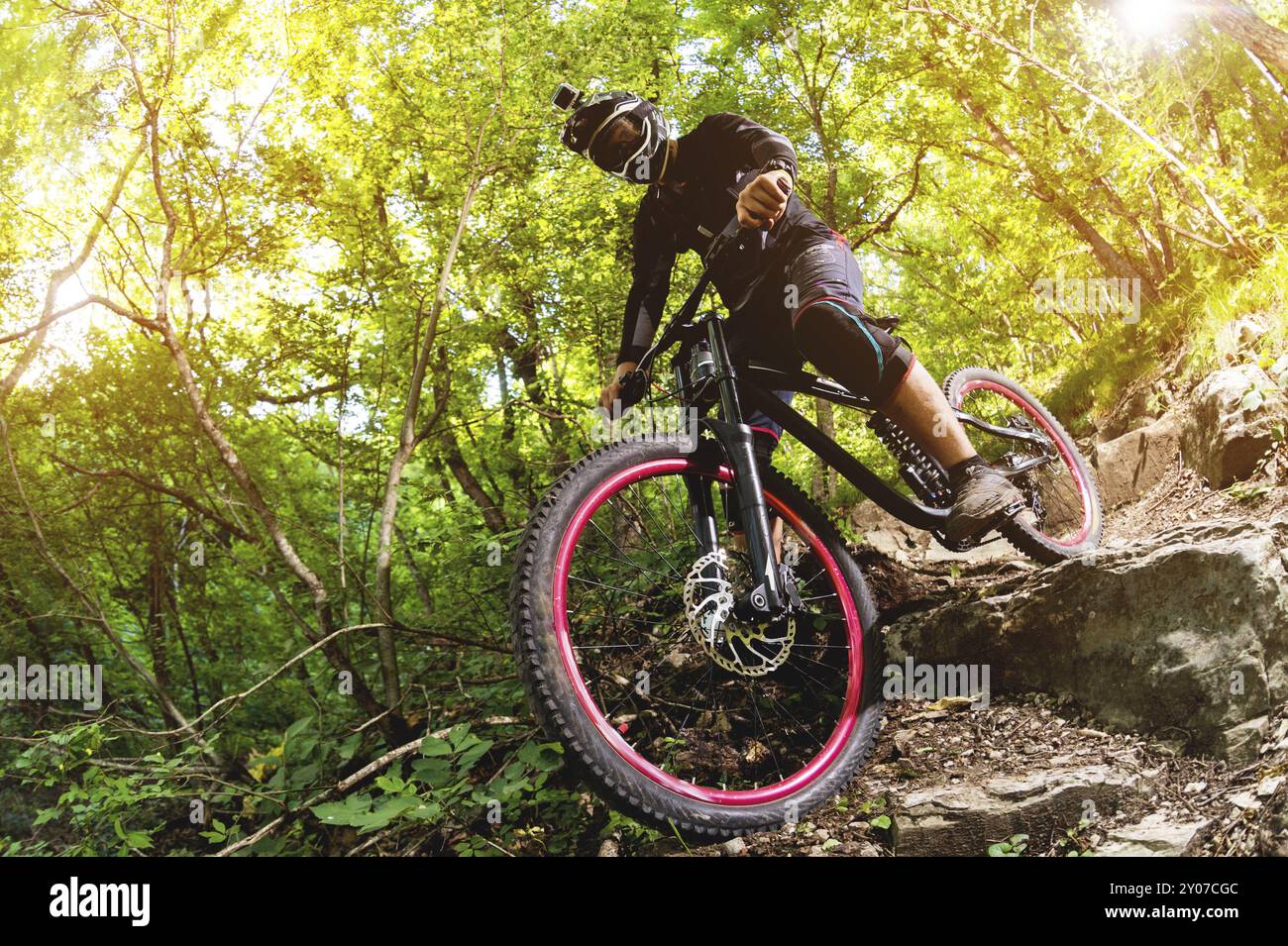 A young rider on a bicycle for downhill descends the rocks in the ...