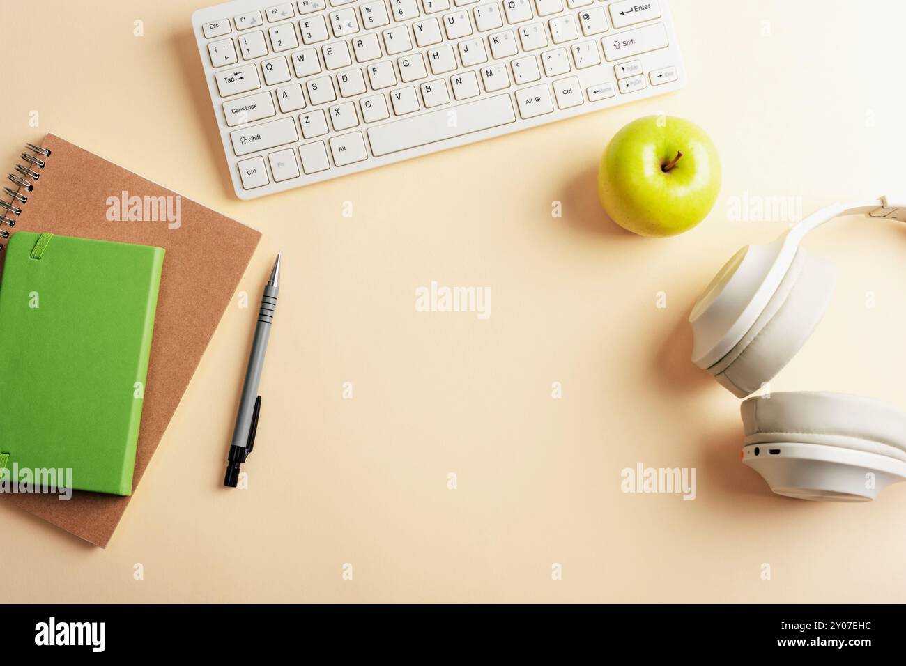 Headphones, keyboard, notepad, pen and green apple on neutral beige ...