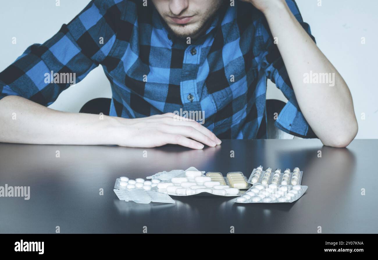 Drug abuse: Young man sitting on a table, drugs and pills in front of ...