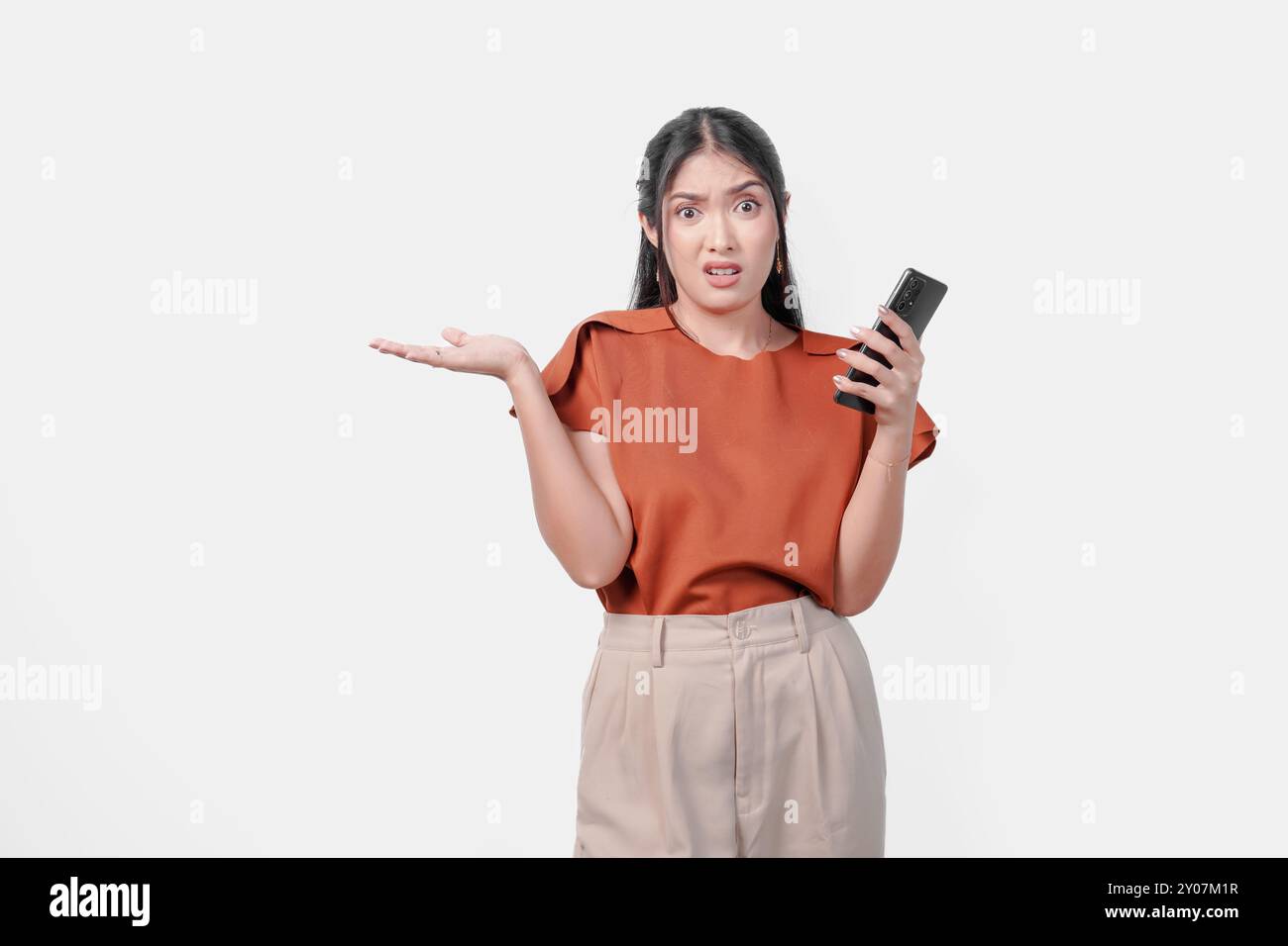 Confused young Asian woman in an brown shirt holding a smartphone with ...