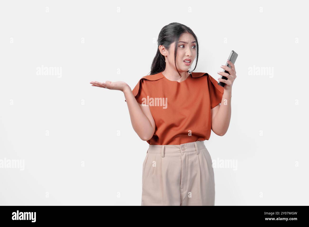 Confused young Asian woman in an brown shirt holding a smartphone with ...