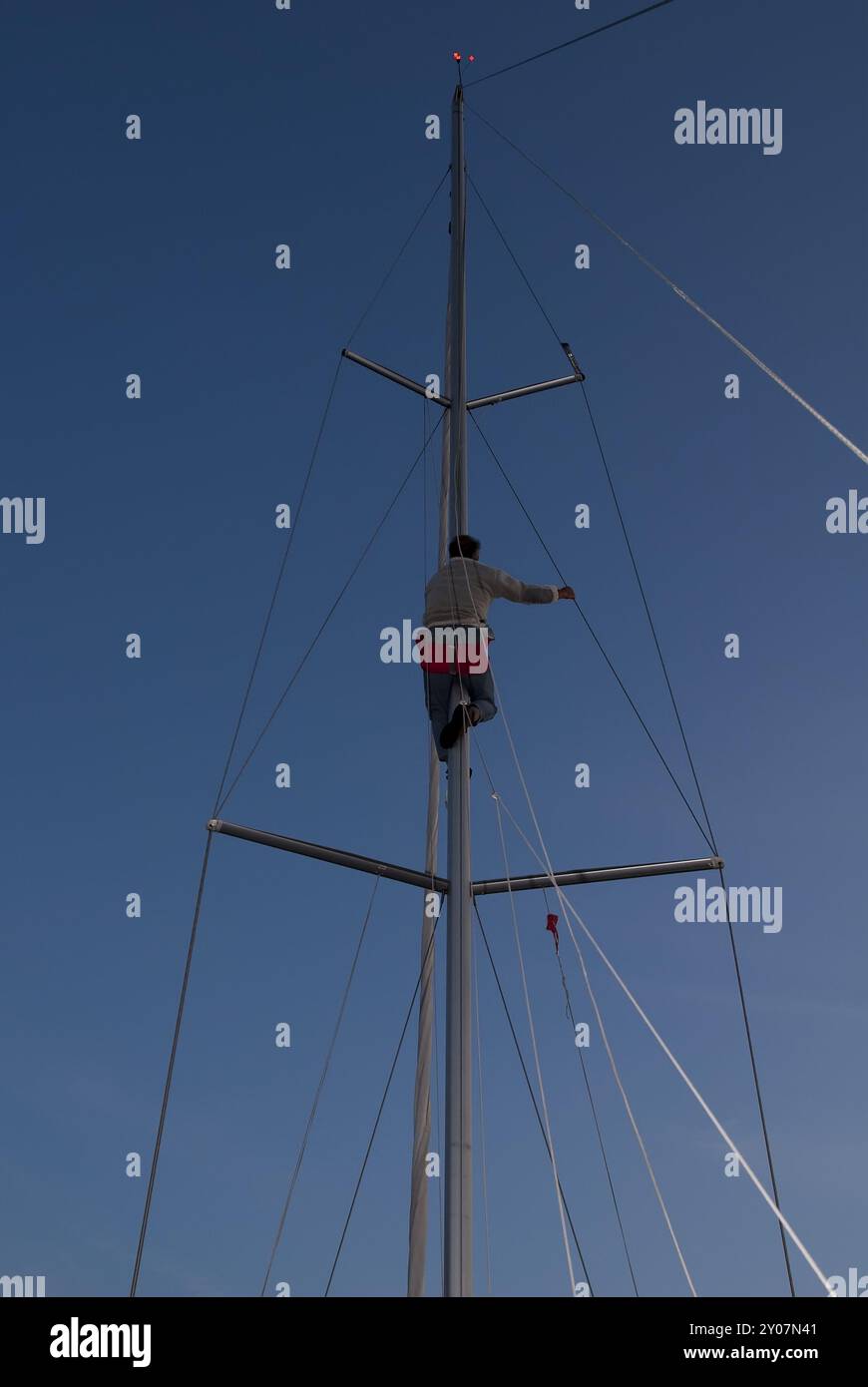 Man sitting in a bosun's chair at the main mast of a sailing yacht ...