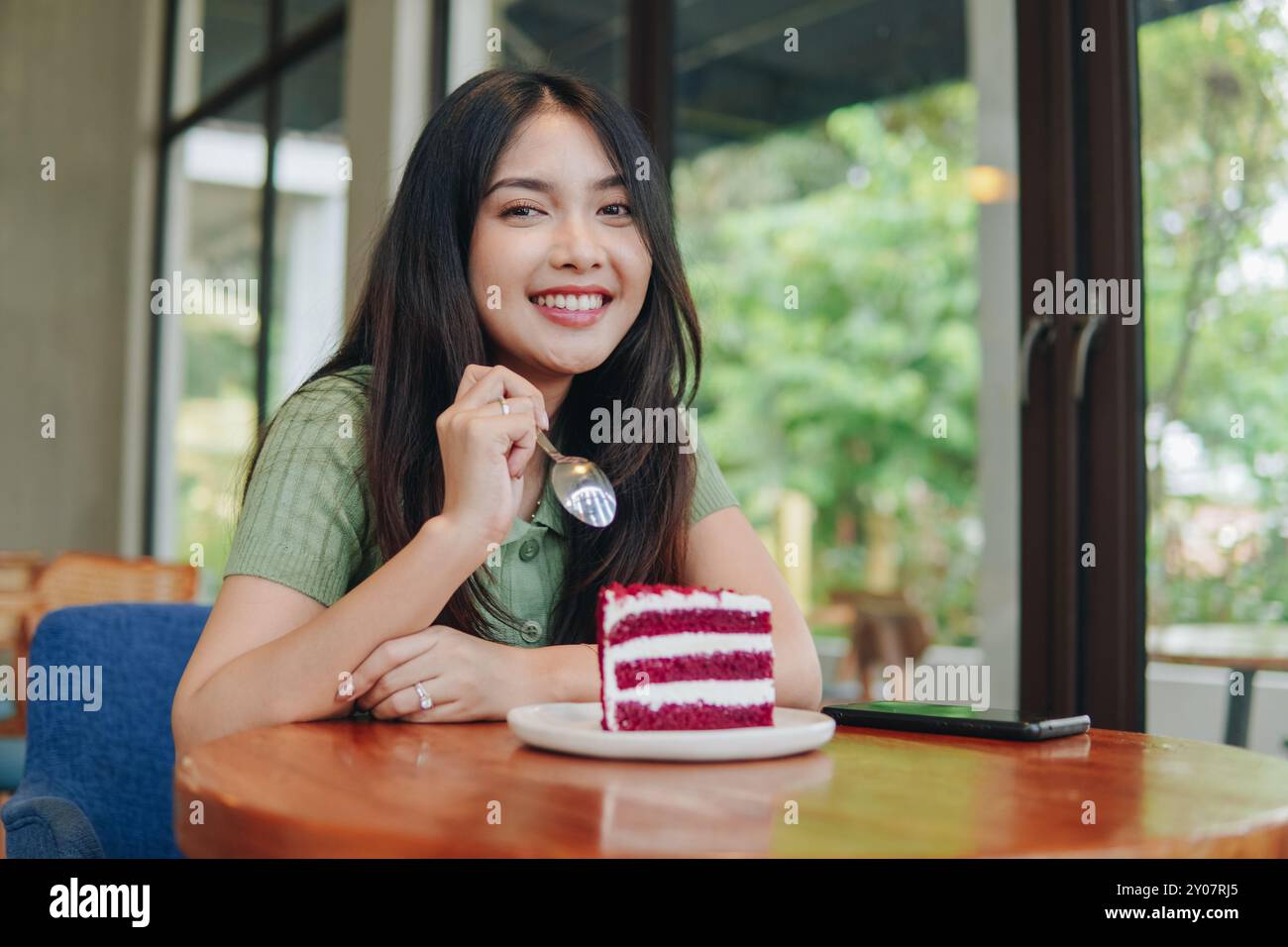 A woman is eating a slice of red velvet cake. She is smiling and she is ...