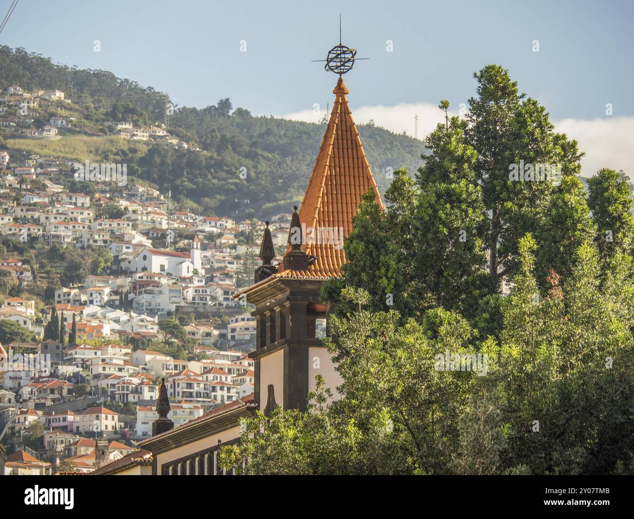 Church spire with red roof and trees against a backdrop of urban hills ...