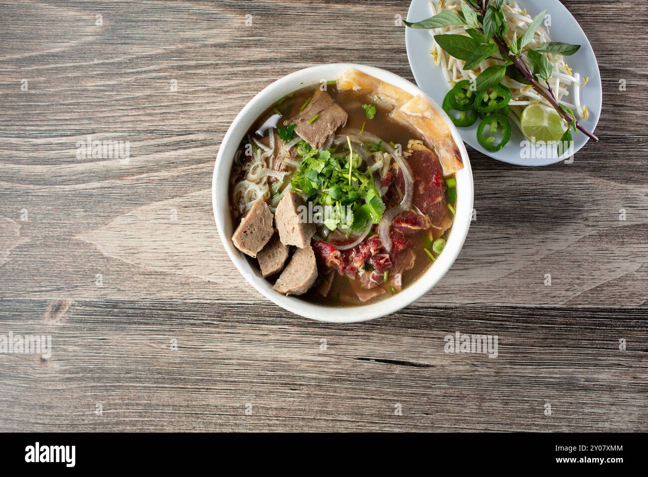 A top down view of a bowl of pho, featuring rare steak, flank, tendon ...