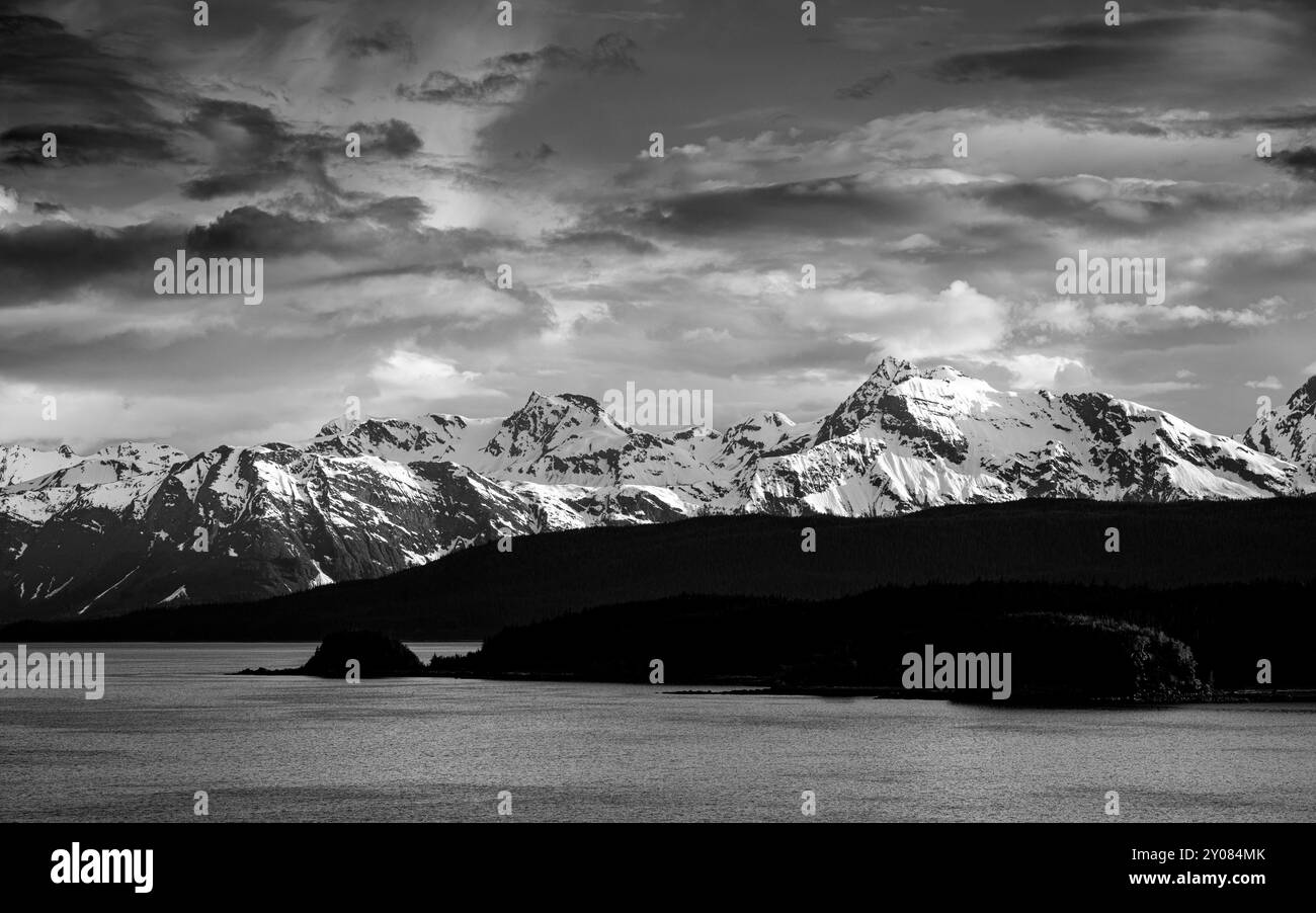 seascape with silhouette tree line against snow capped mountain range ...