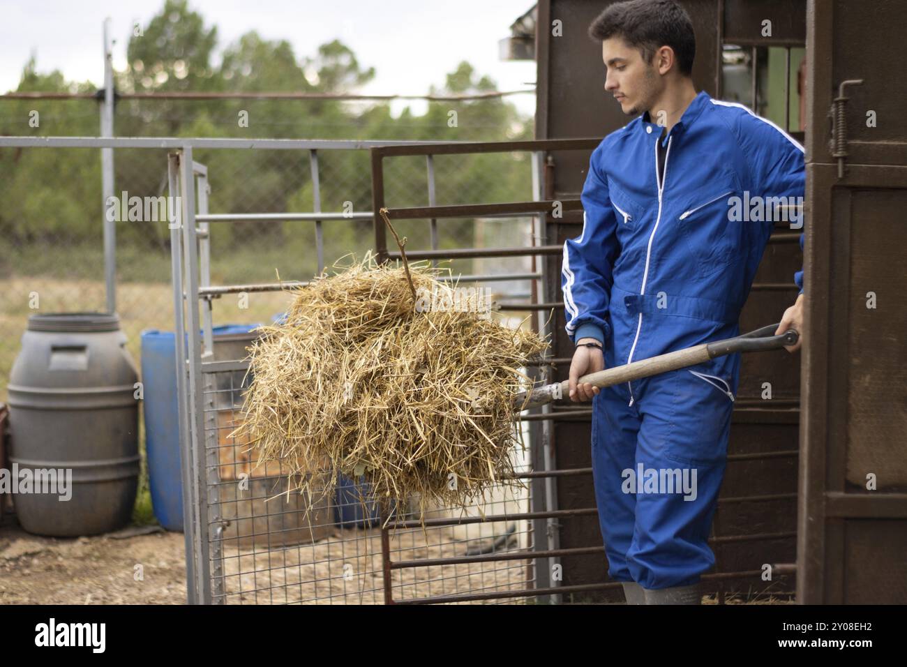 Portrait of young farmer in uniform working on his farm clearing straw ...