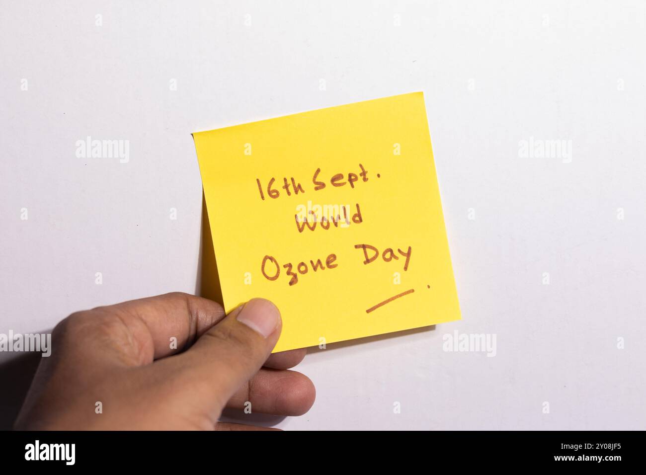 A yellow sticky note held in human hand showing world ozone day on ...