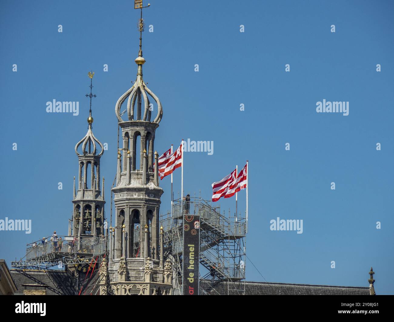 Two spires with waving flags, surrounded by scaffolding, under a clear ...