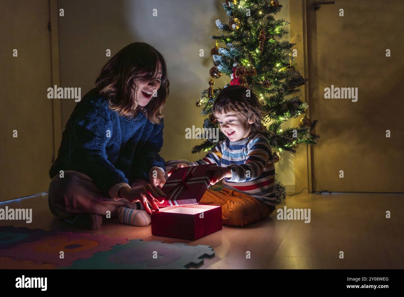 A young boy and girl are sitting on the floor in front of a Christmas ...
