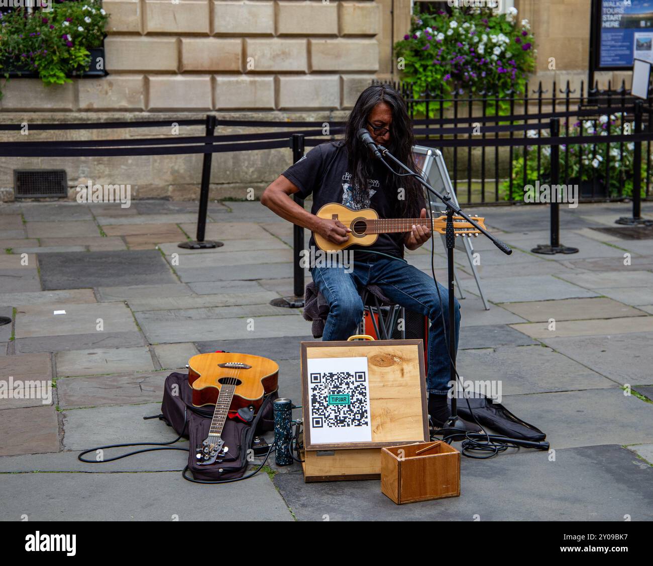 Street musician playing guitar and singing, seated in front of an open ...