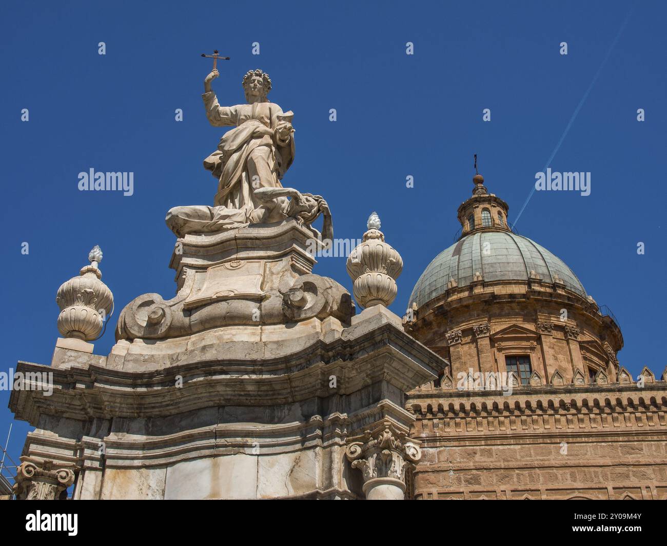 A statue on a pedestal in front of a church dome under a clear blue sky ...