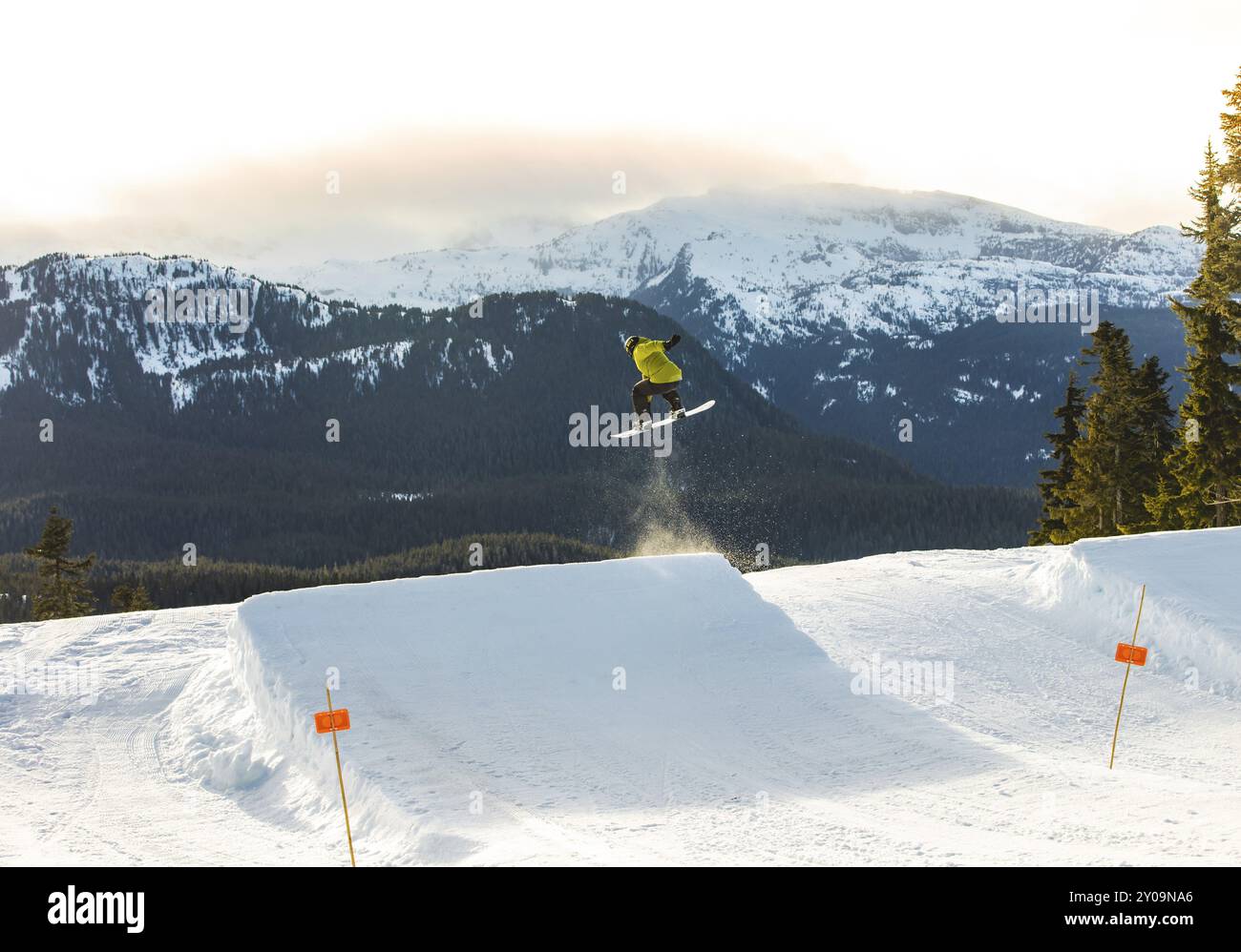 Snowboarder mid-jump on a snowy mountain slope with evergreen trees and ...