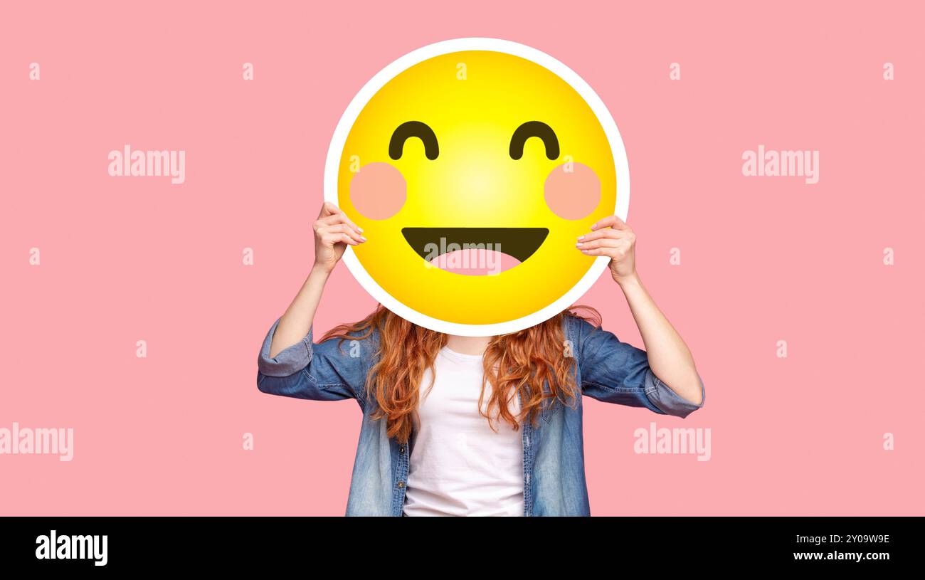 Redhead girl hiding her face behind happy emoji smile Stock Photo - Alamy