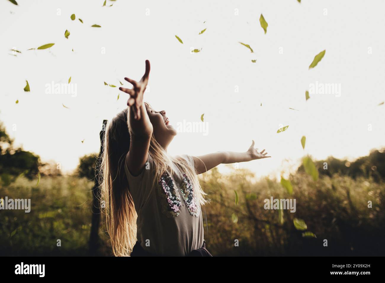 Happy little blonde girl plays with green leaves in garden, field. The ...