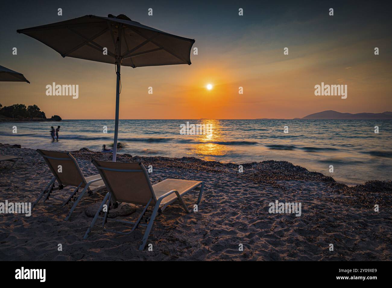 Beach scene with sunset, deckchairs and parasol in warm colours ...