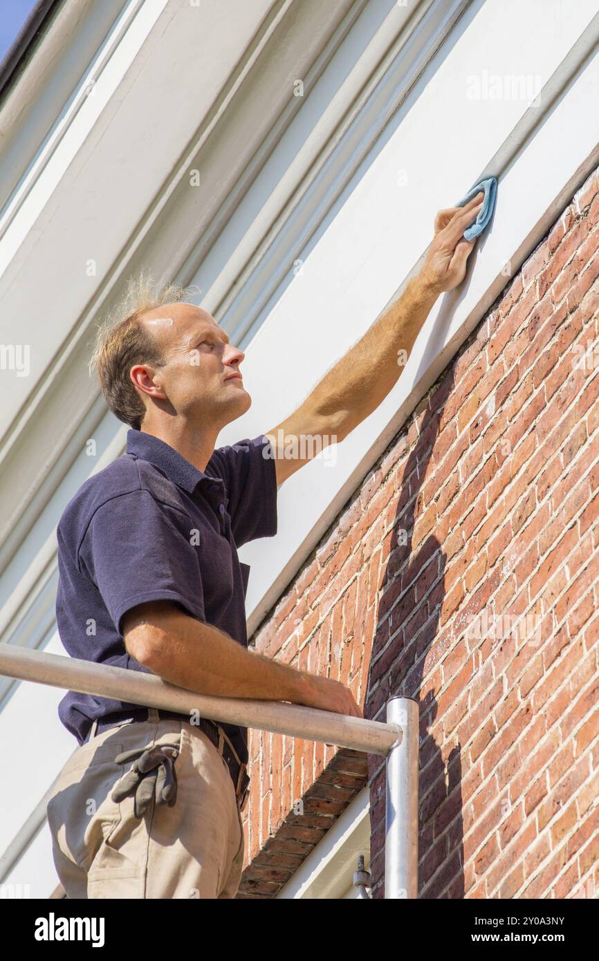 Dutch painter working on scaffolding cleaning roof molding with cloth ...