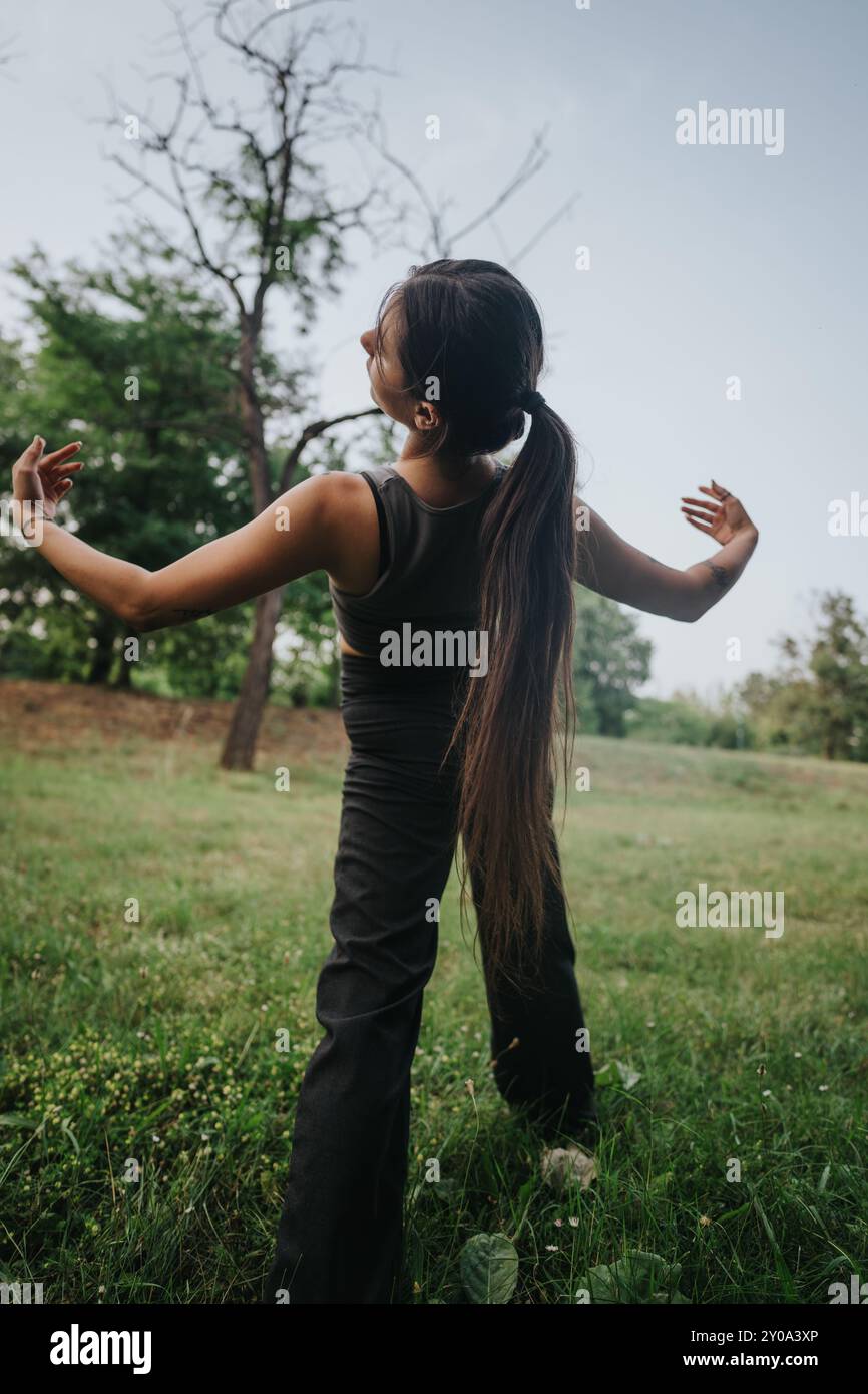 Young girl dancing gracefully in a serene park setting surrounded by lush greenery and trees ...