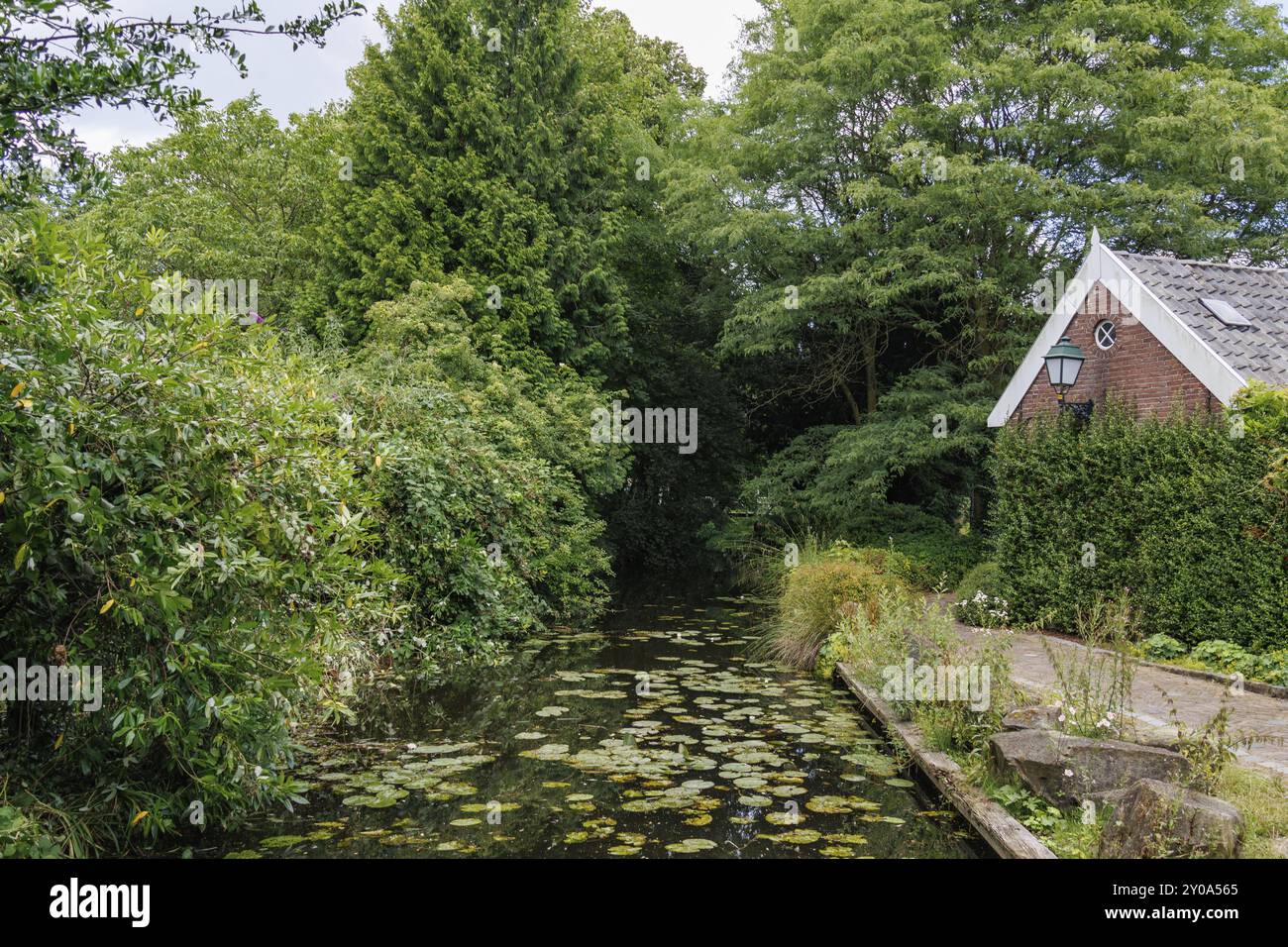 A small brick house on the riverbank with water lilies and surrounded ...