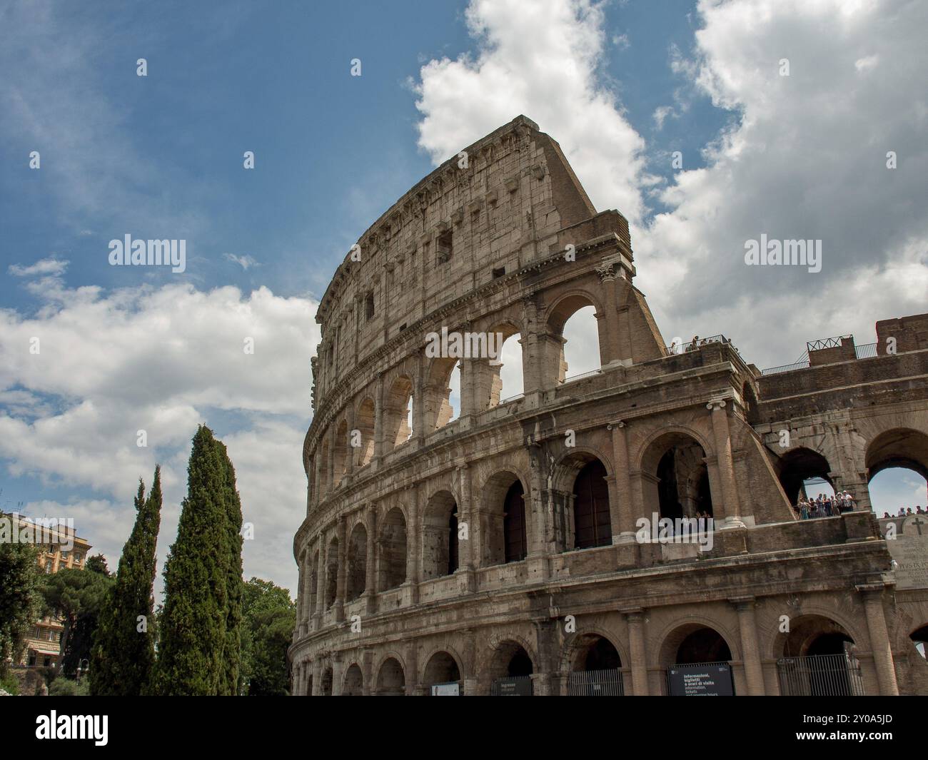 Side view of the imposing Colosseum with high arcades and trees under a ...