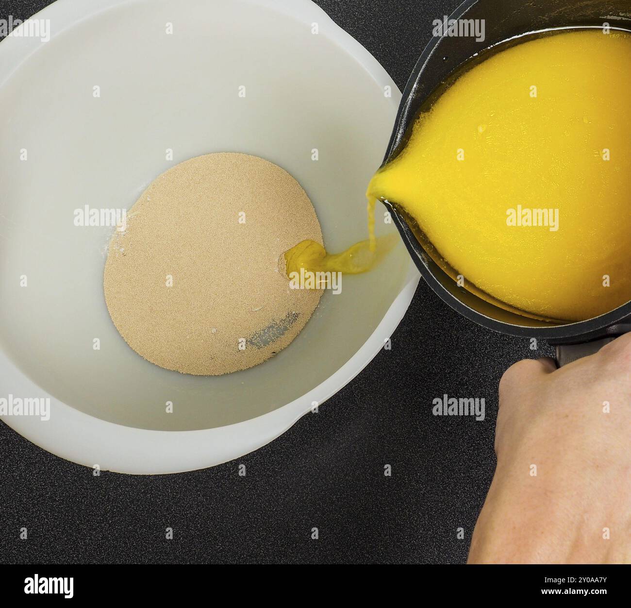 Hand pouring melted butter from black kettle into a white bowl of dry ...