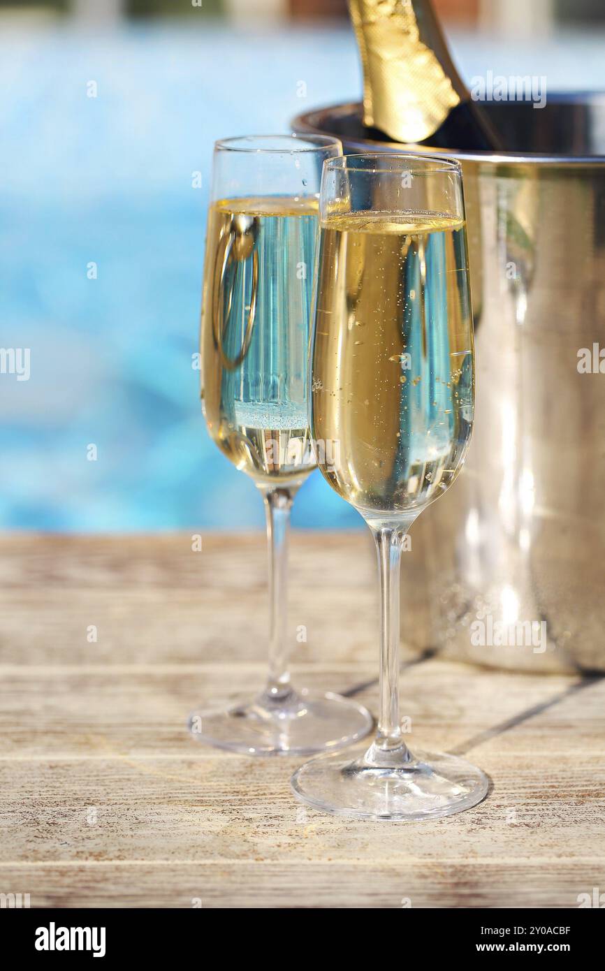 Champagne glasses and bottle in ice bucket near swimming pool. Vacation ...