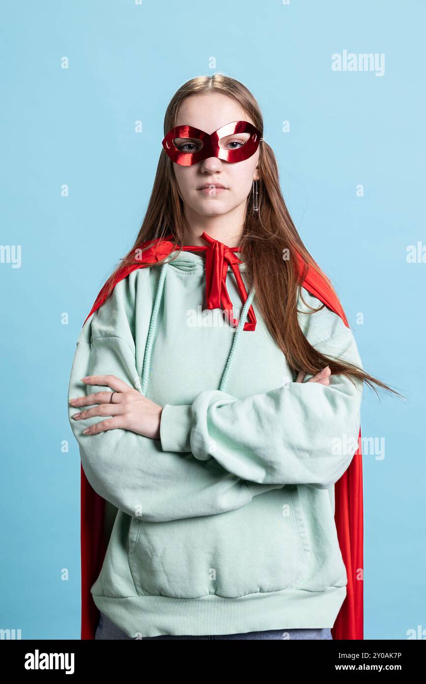 Young girl with mask portraying superhero, wearing red cape, isolated ...