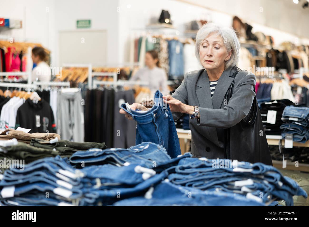 Old woman customer choosing jean skirt in clothing store Stock Photo ...