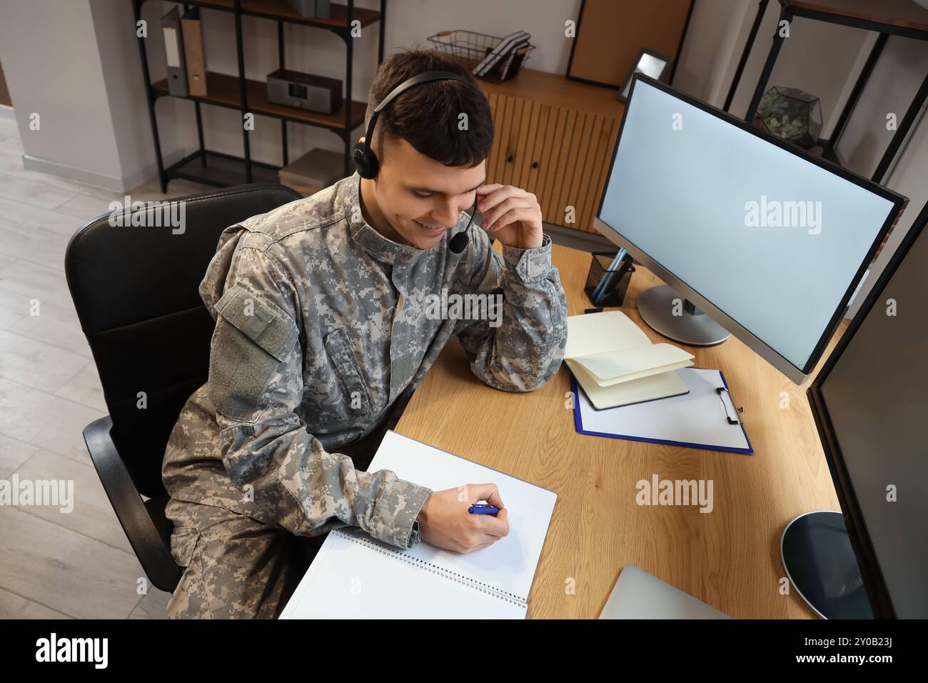 Young male soldier in headset working with computer and journal at ...