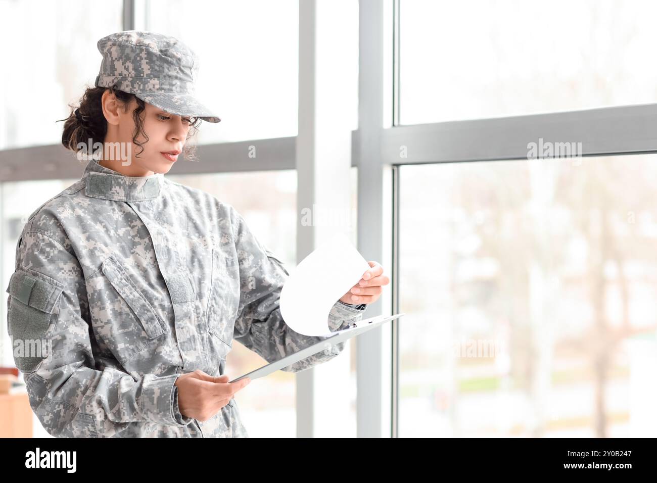 Female African-American soldier with clipboard near window at ...