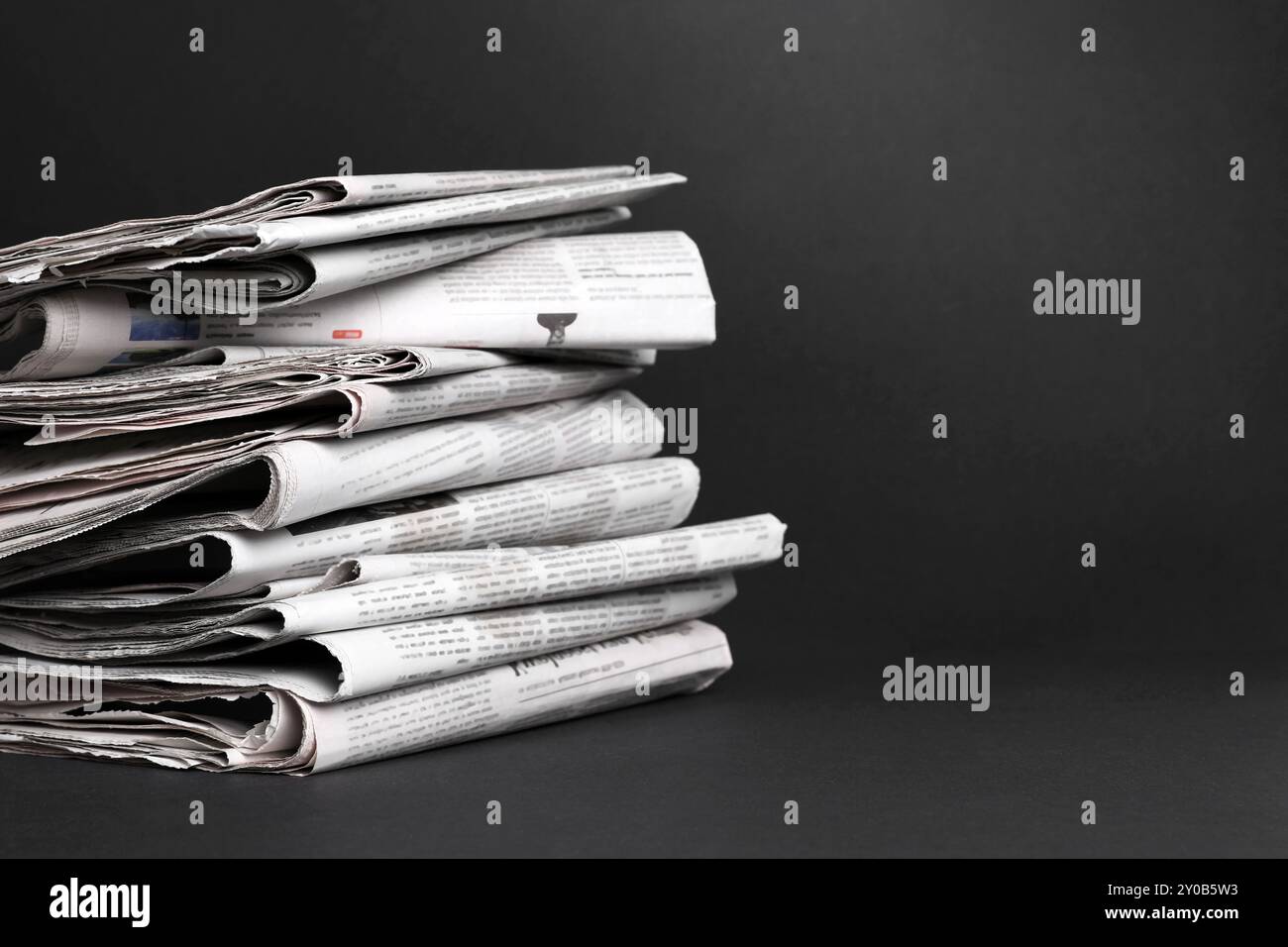 Stack of newspapers in different languages on black background. Space ...