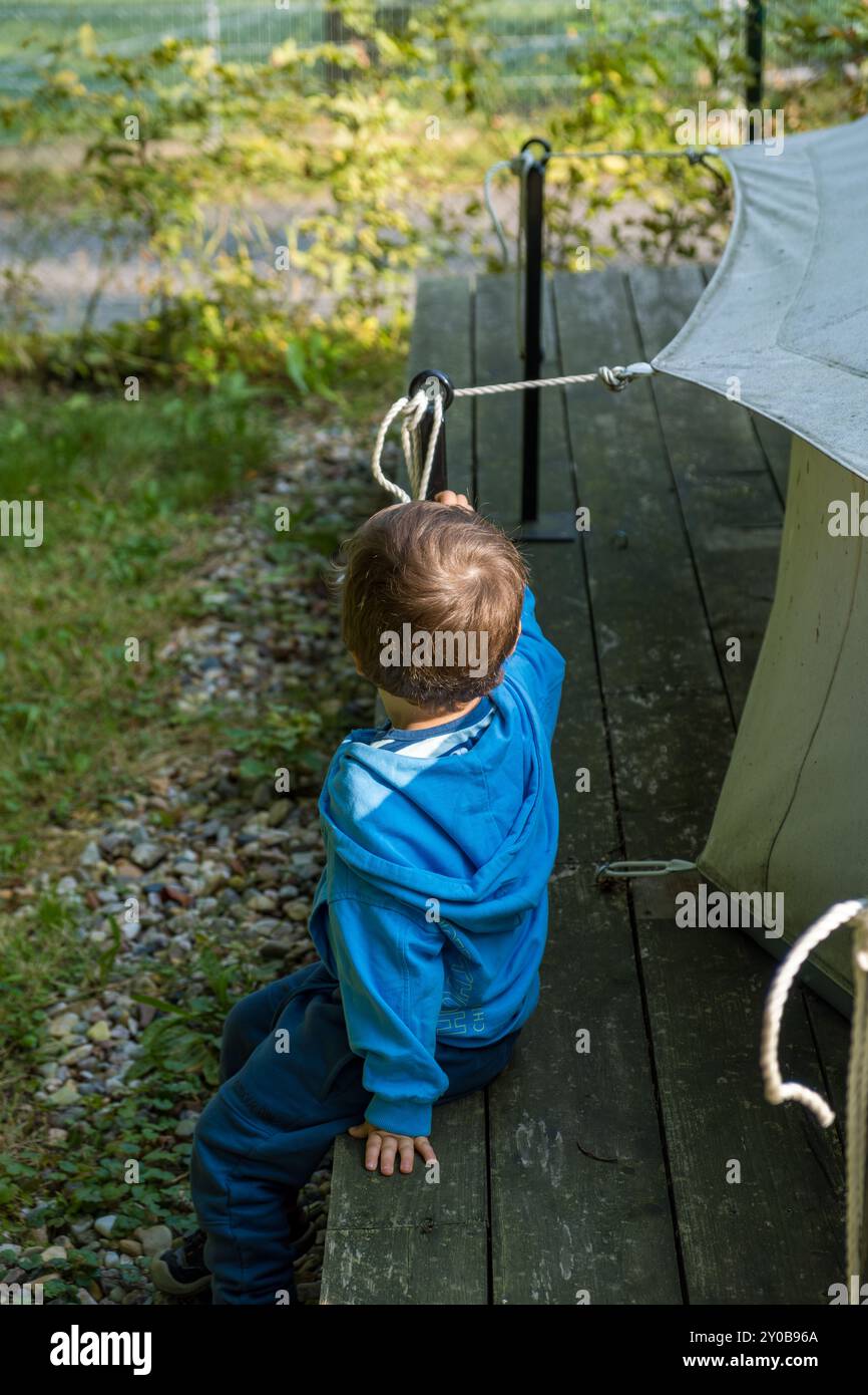 Boy sitting in camping tents set up in a forest with wooden platforms ...